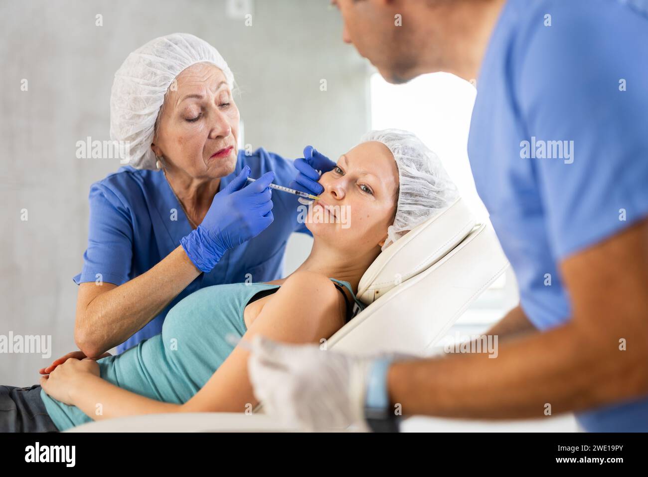 Elderly female doctor and male assistant gives injection of botulinum ...