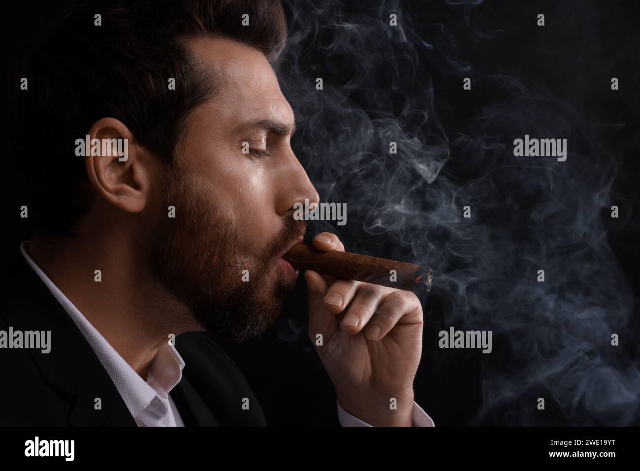 Handsome man smoking cigar on black background. Space for text Stock ...