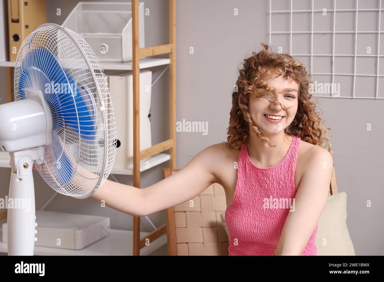 Beautiful happy young woman with electric fan sitting on chair in ...