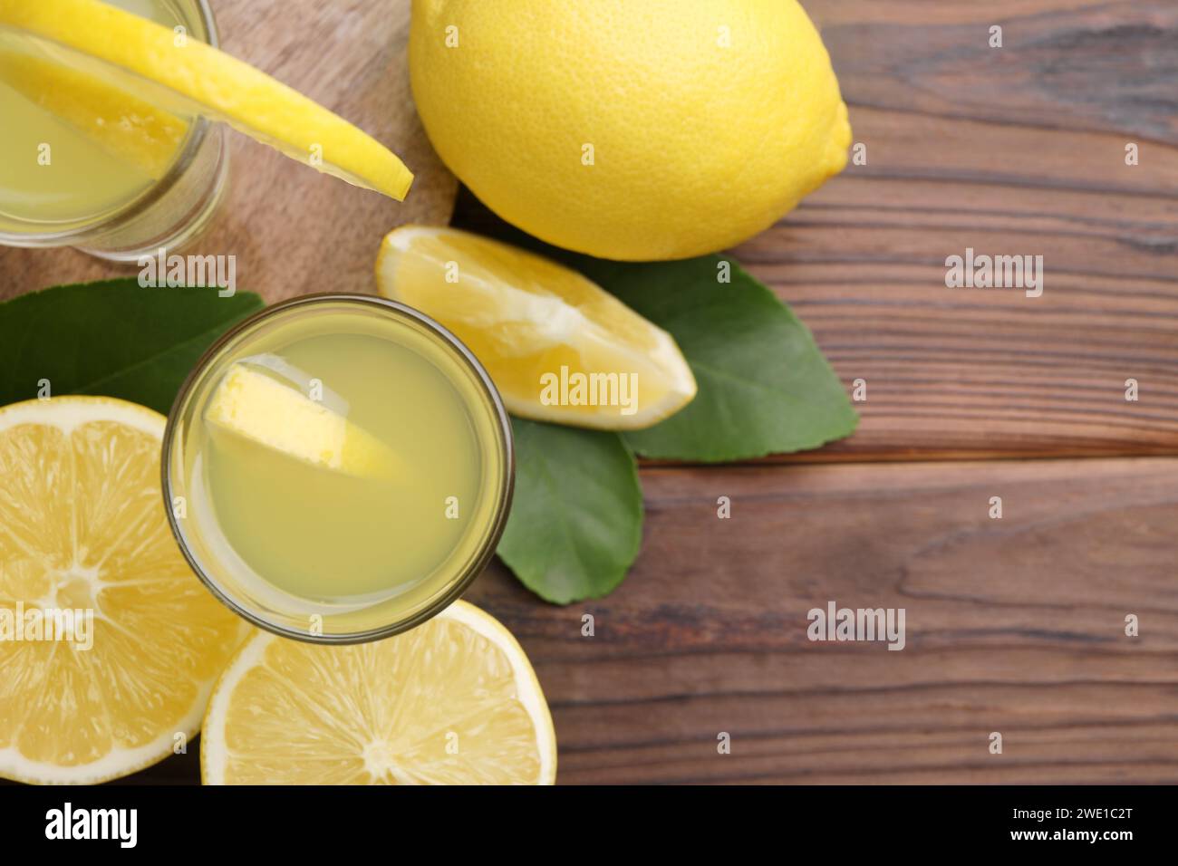 Tasty limoncello liqueur, lemons and green leaves on wooden table, top ...
