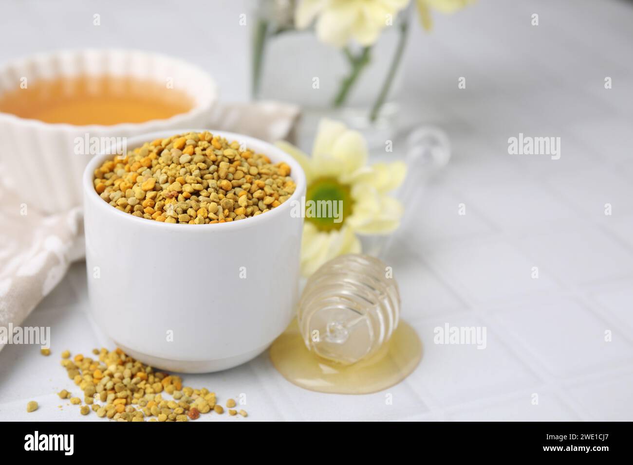Fresh bee pollen granules and dipper with honey on white tiled table ...