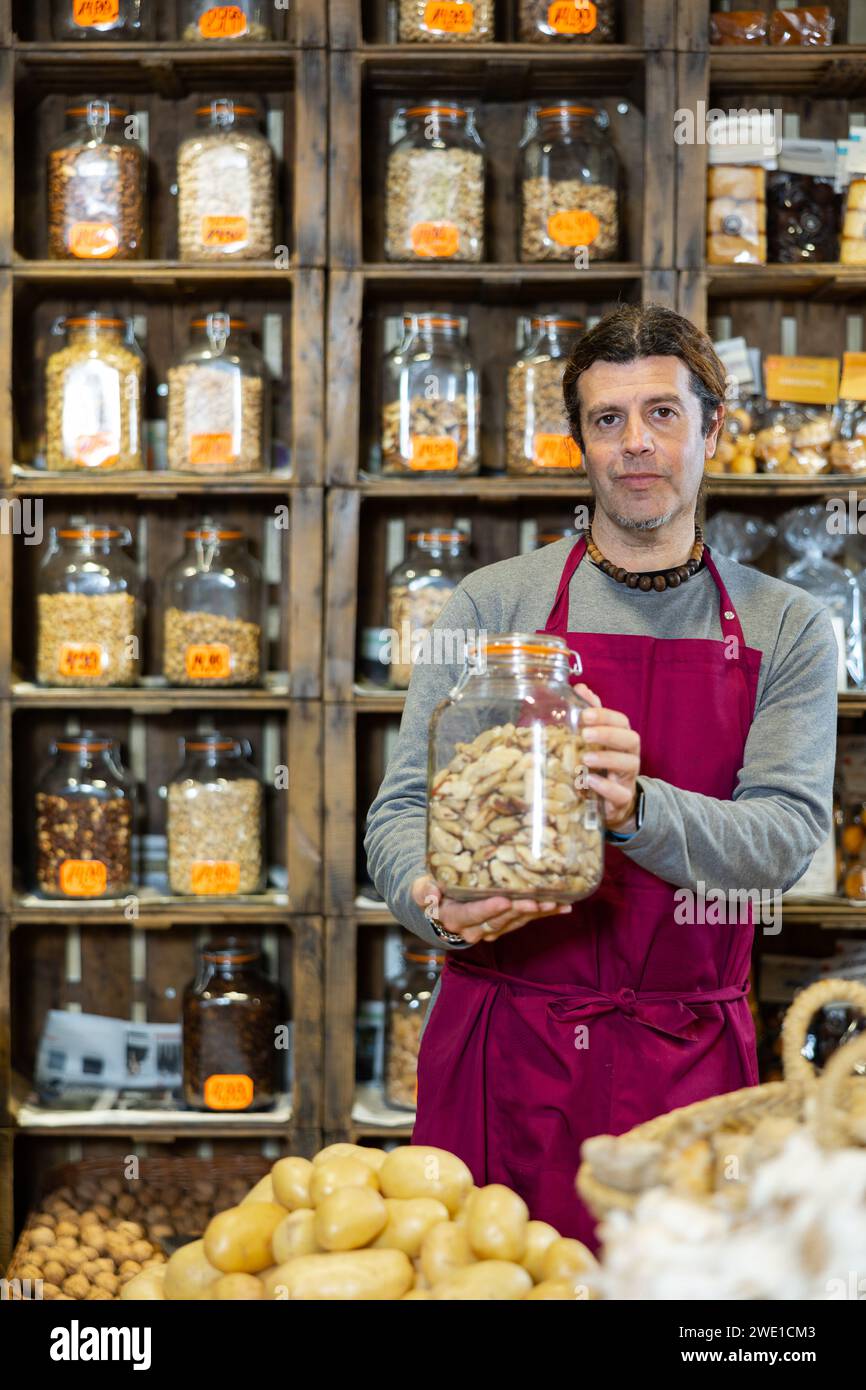 Male seller holding jar of brazil nuts standing in nut section of ...