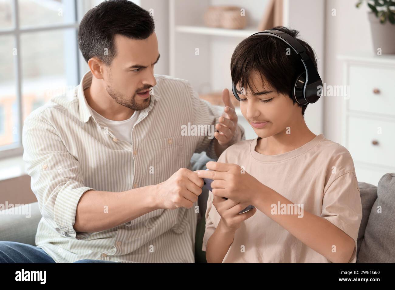 Angry father taking mobile phone away from his teenage son at home ...