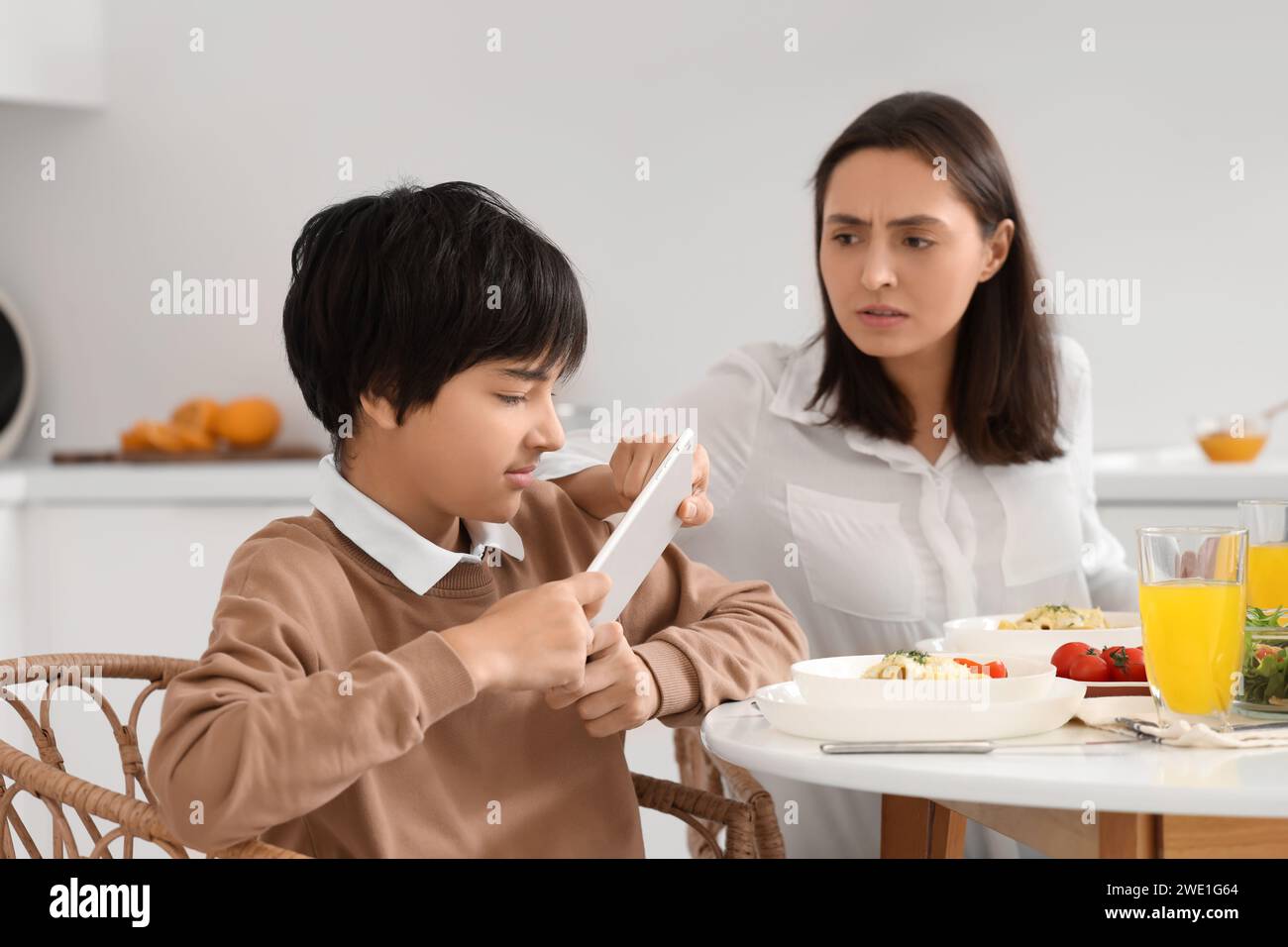 Angry mother taking tablet computer away from her teenage son at table ...