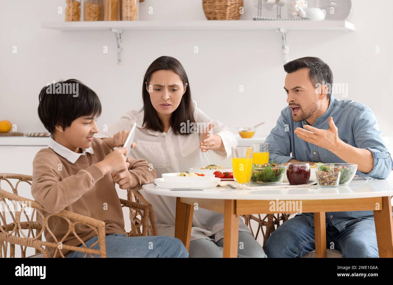 Teenage boy using tablet computer and his angry parents at table during ...