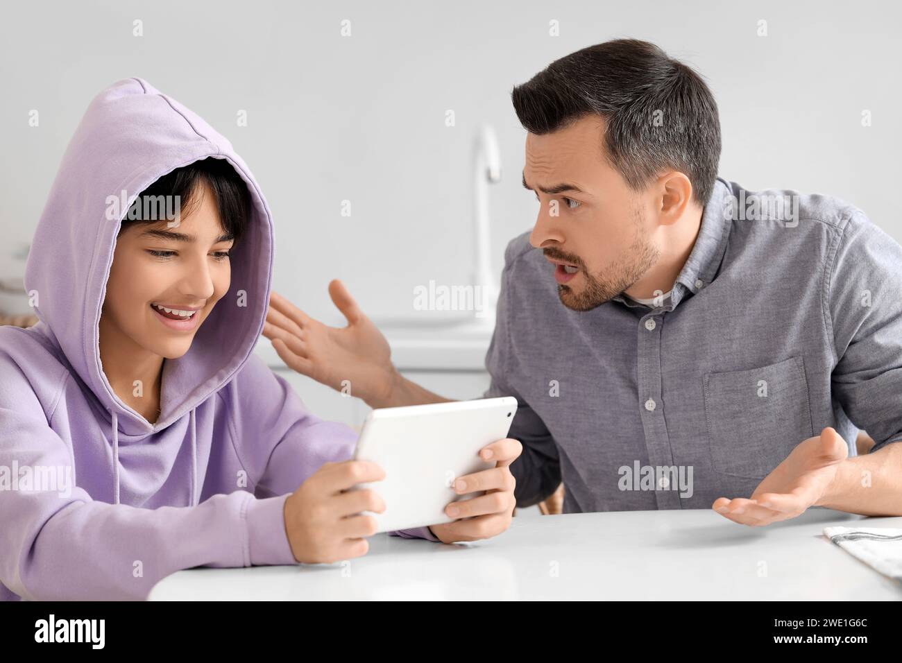 Teenage boy using tablet computer and his angry father in kitchen ...