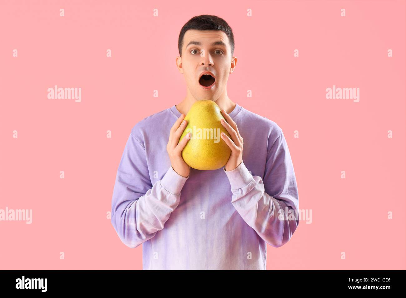 Shocked young man with pomelo on pink background Stock Photo - Alamy