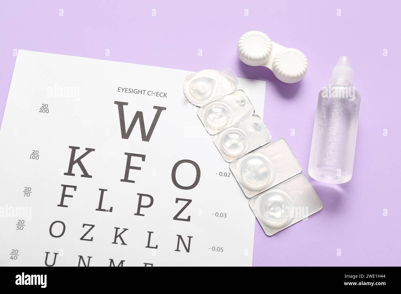 Eye test chart with container, solution and contact lenses on lilac ...