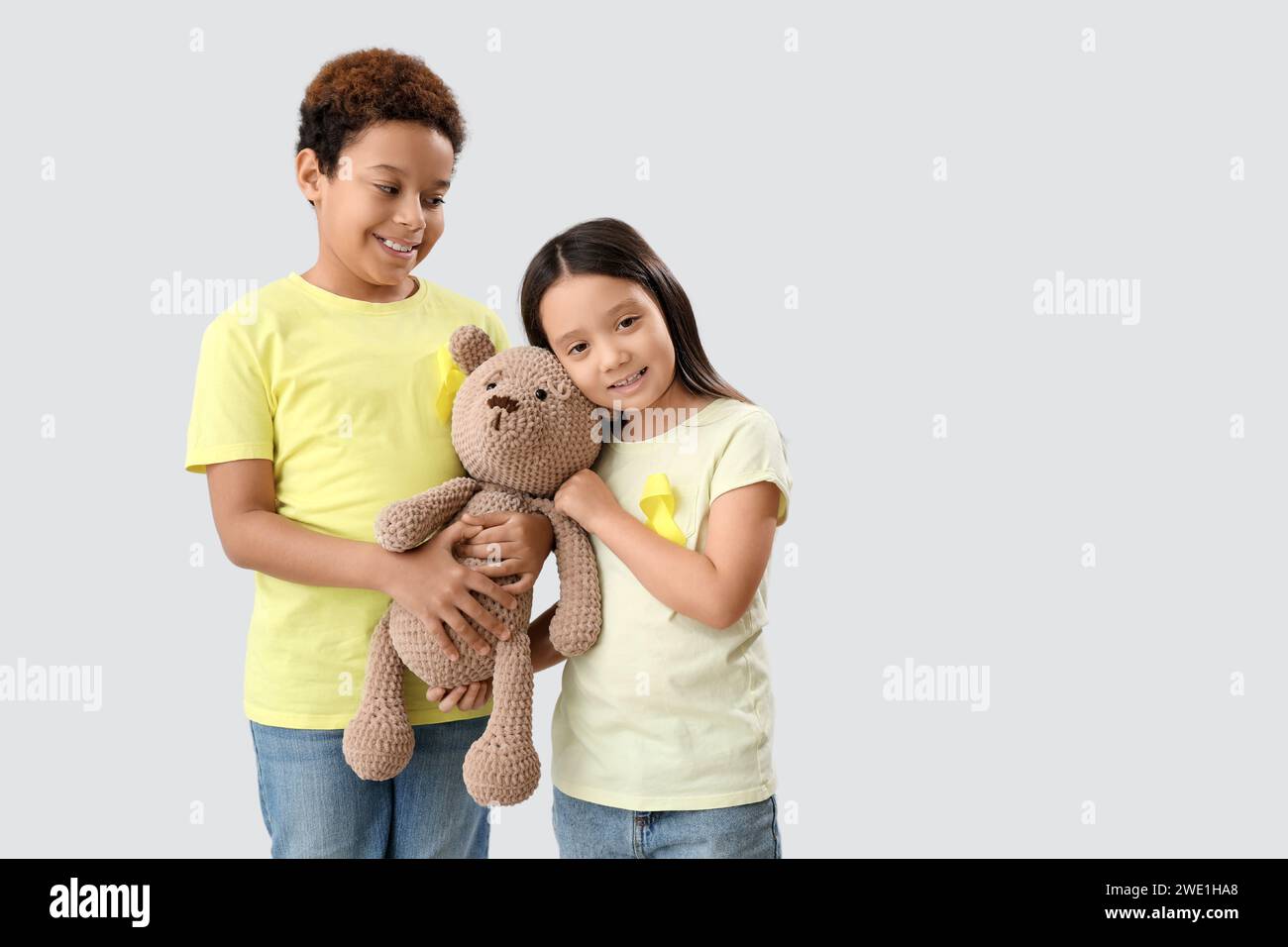 Cute little children with yellow ribbons and teddy bear on grey ...