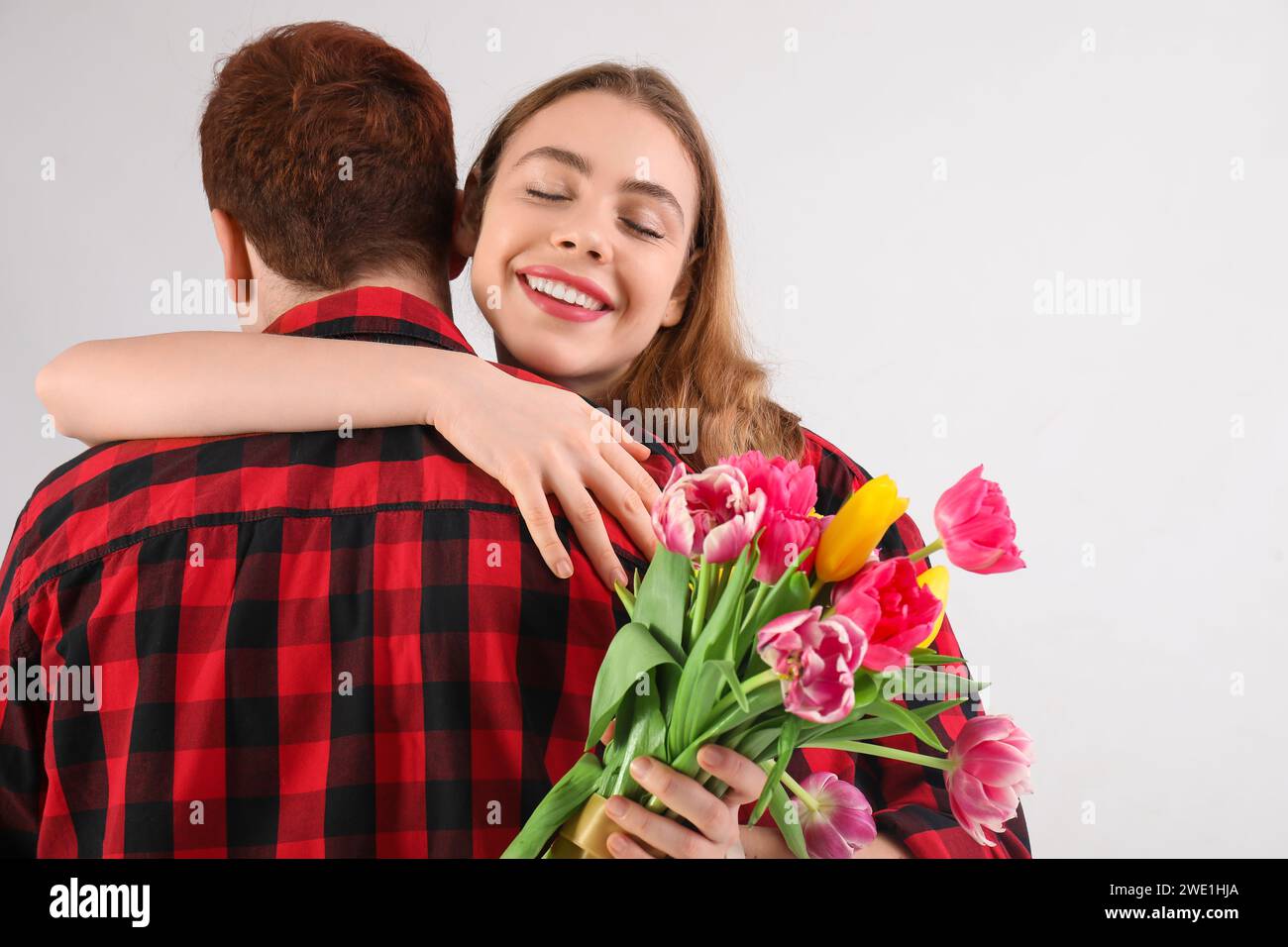 Happy young woman with tulip flowers hugging her boyfriend on white background Stock Photo - Alamy