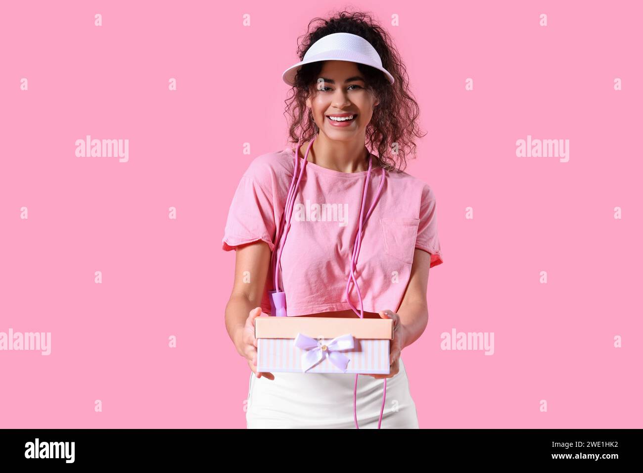 Young African-American woman in sportswear with skipping rope, gift box ...