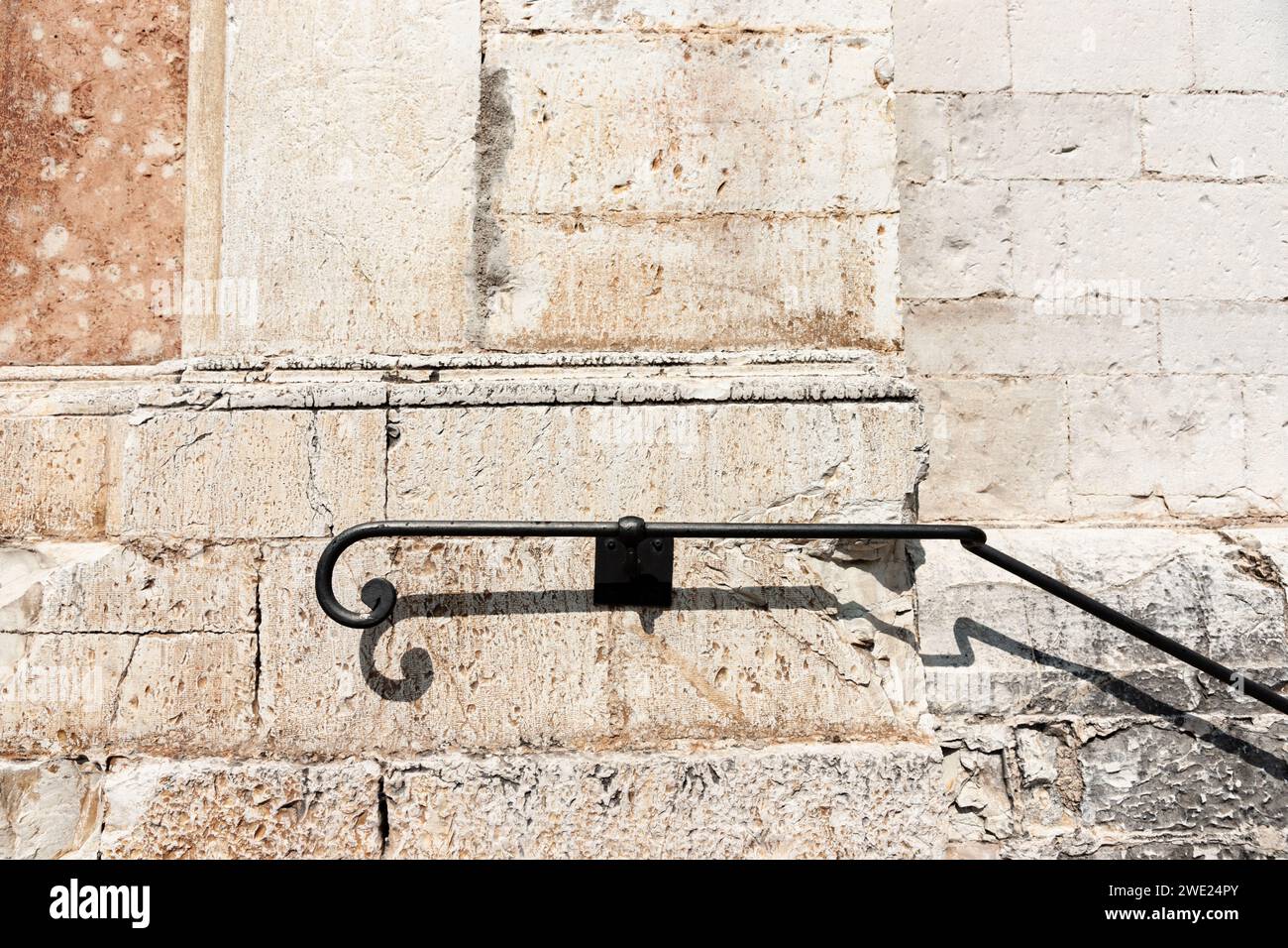Black wrought iron handrail and parallel shadow on exterior stone wall ...