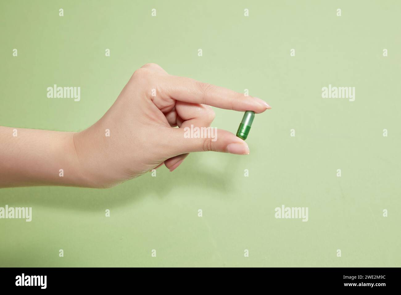 A female hand holding a single a green capsule of vitamin on a light ...