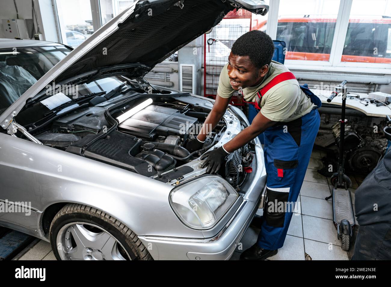 Young African man working under the hood of car fixing engine in auto ...
