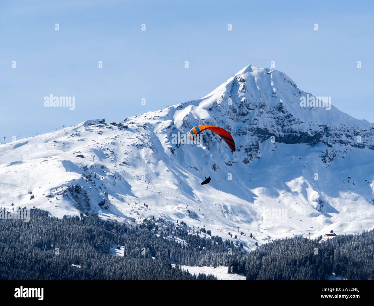 A lone paraglider soars gracefully over majestic snow-covered mountains ...