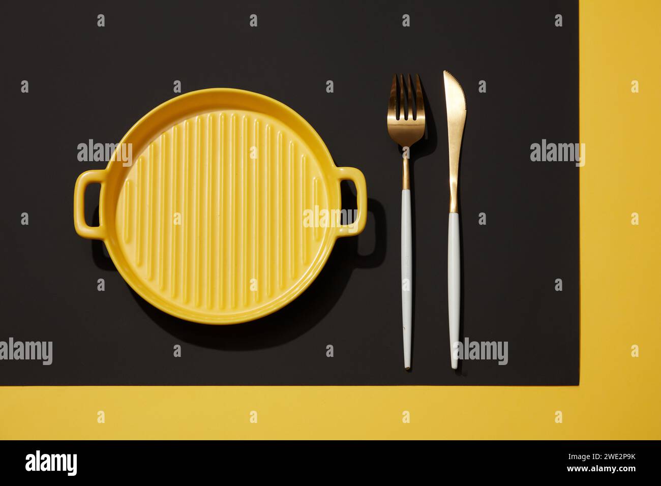 Top view of yellow pan with knife and fork displayed on black and ...