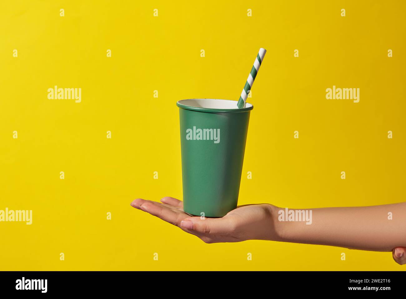 A green disposable paper cup with a paper straw placed in a woman's ...
