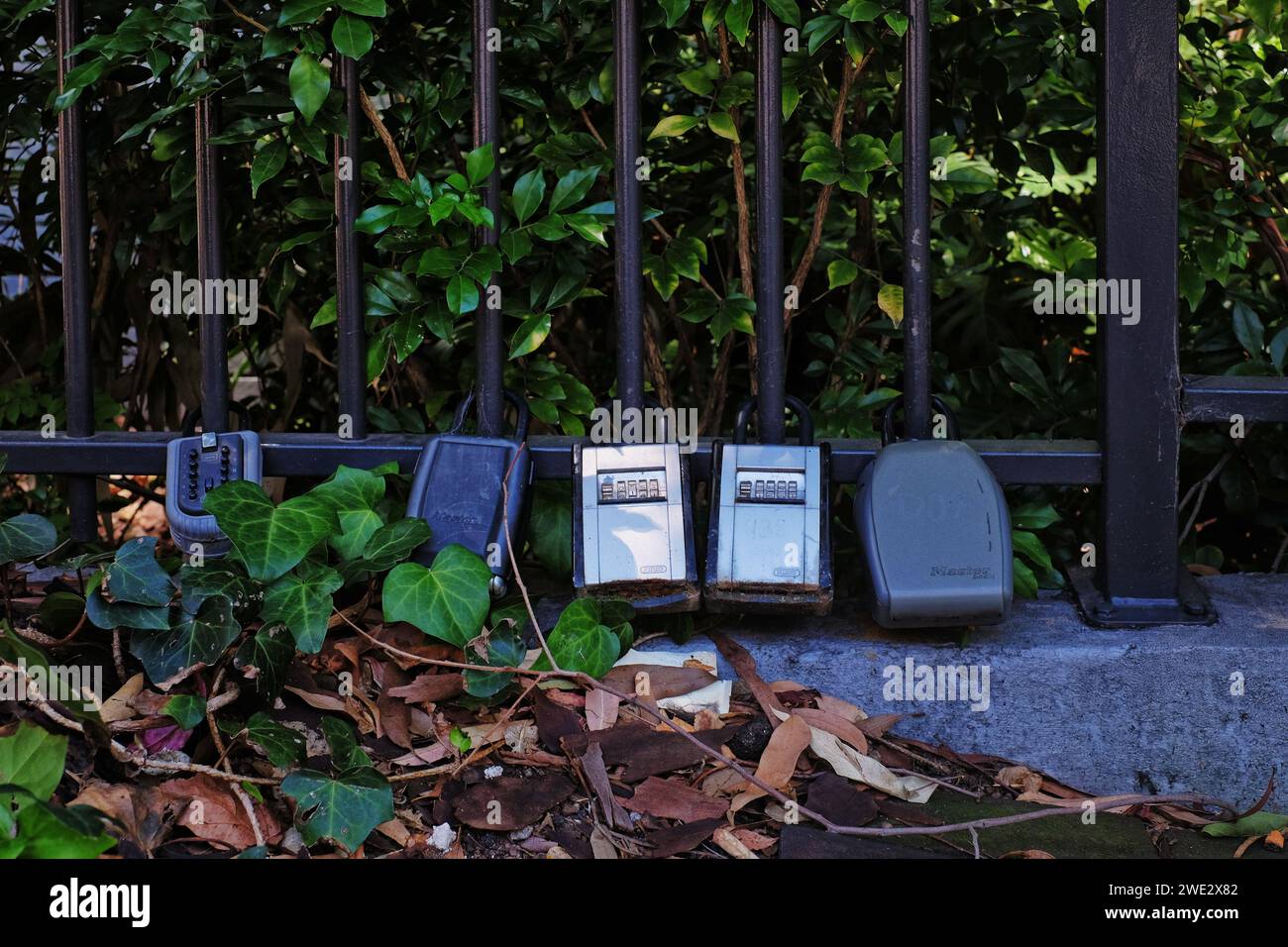A row of key boxes attached to a metal palisade fence at ground level ...