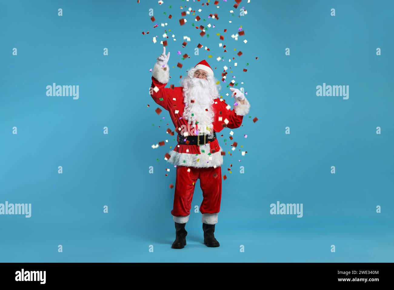 Santa Claus under falling confetti on light blue background Stock Photo ...