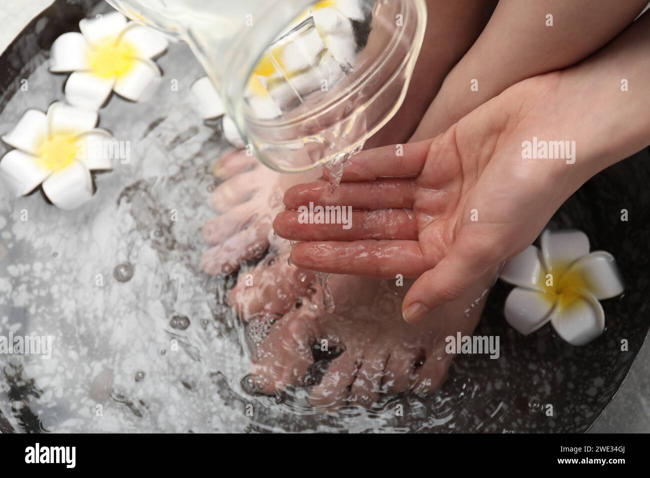Woman pouring water onto hand while soaking her feet in bowl, above ...
