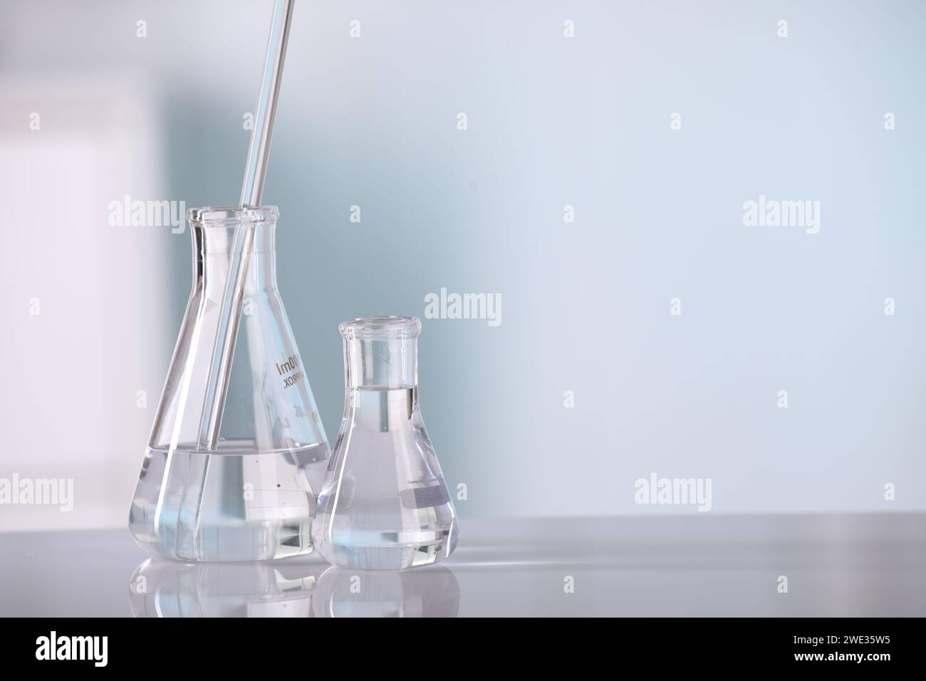Laboratory analysis. Glass flasks and stirring rod on white table ...