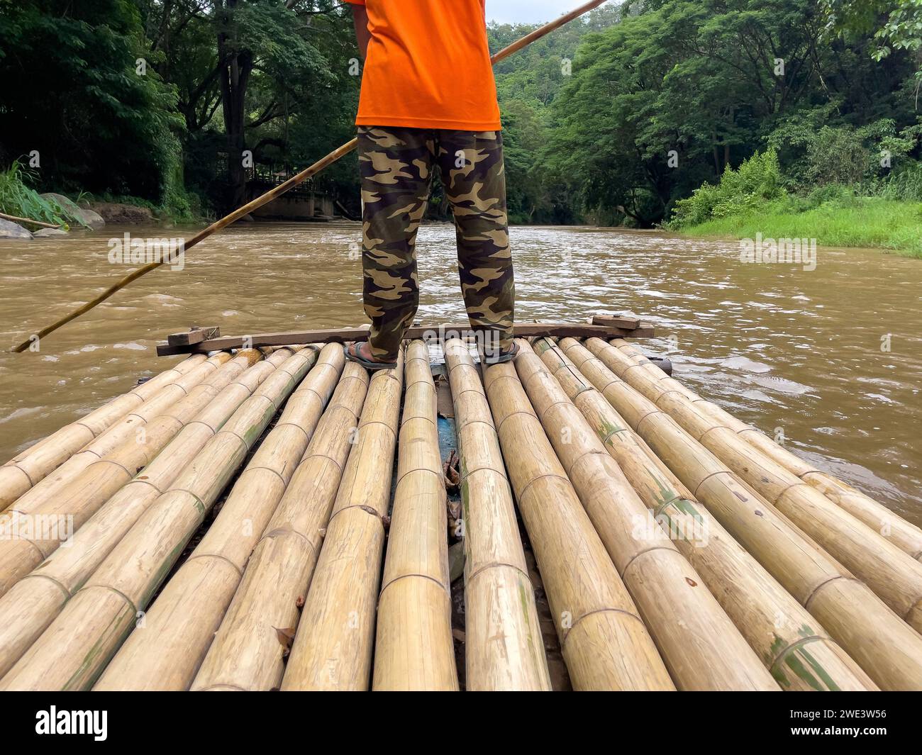 Man rowing bamboo raft. Man uses a bamboo to push a raft on a river and ...