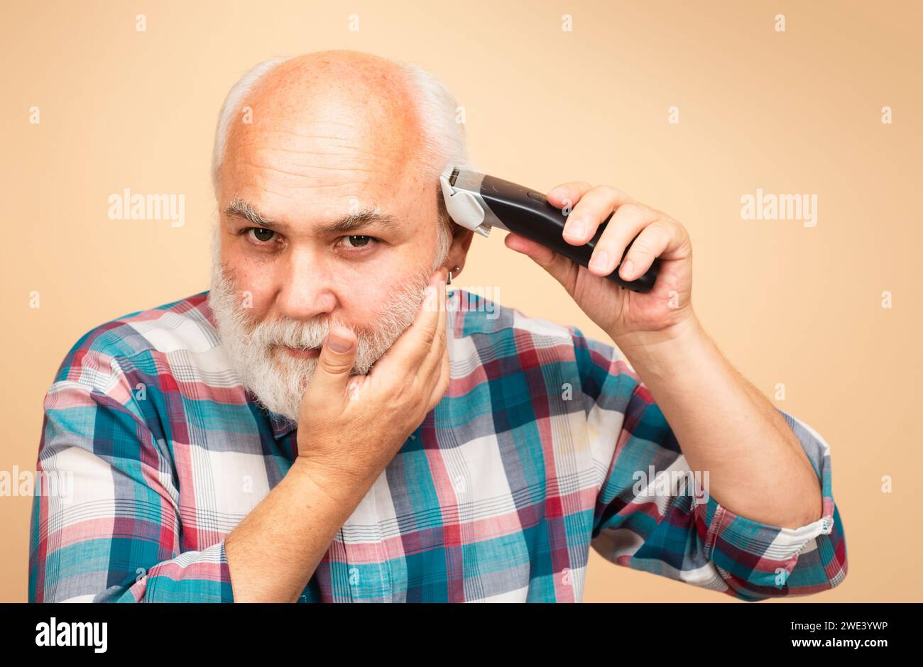 Portrait of old man being trimmed with hair clipper in barbershop ...