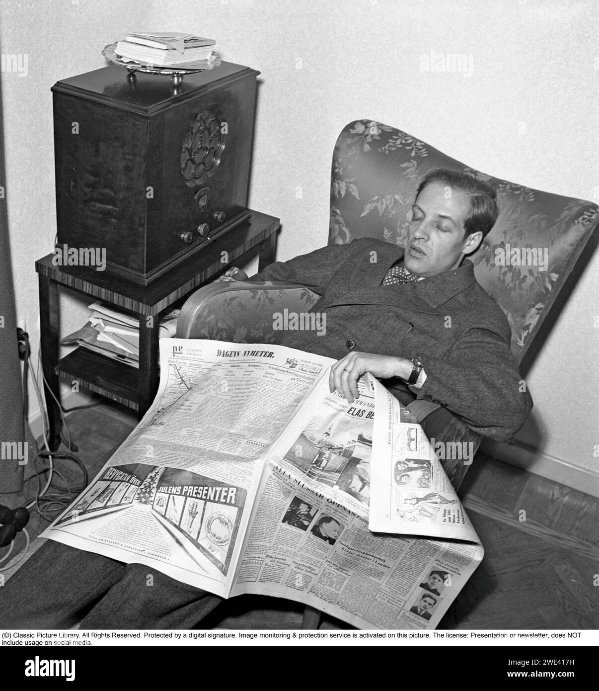 Radio listener in the 1940s. A man manages to fall asleep while reading the paper and listening ...