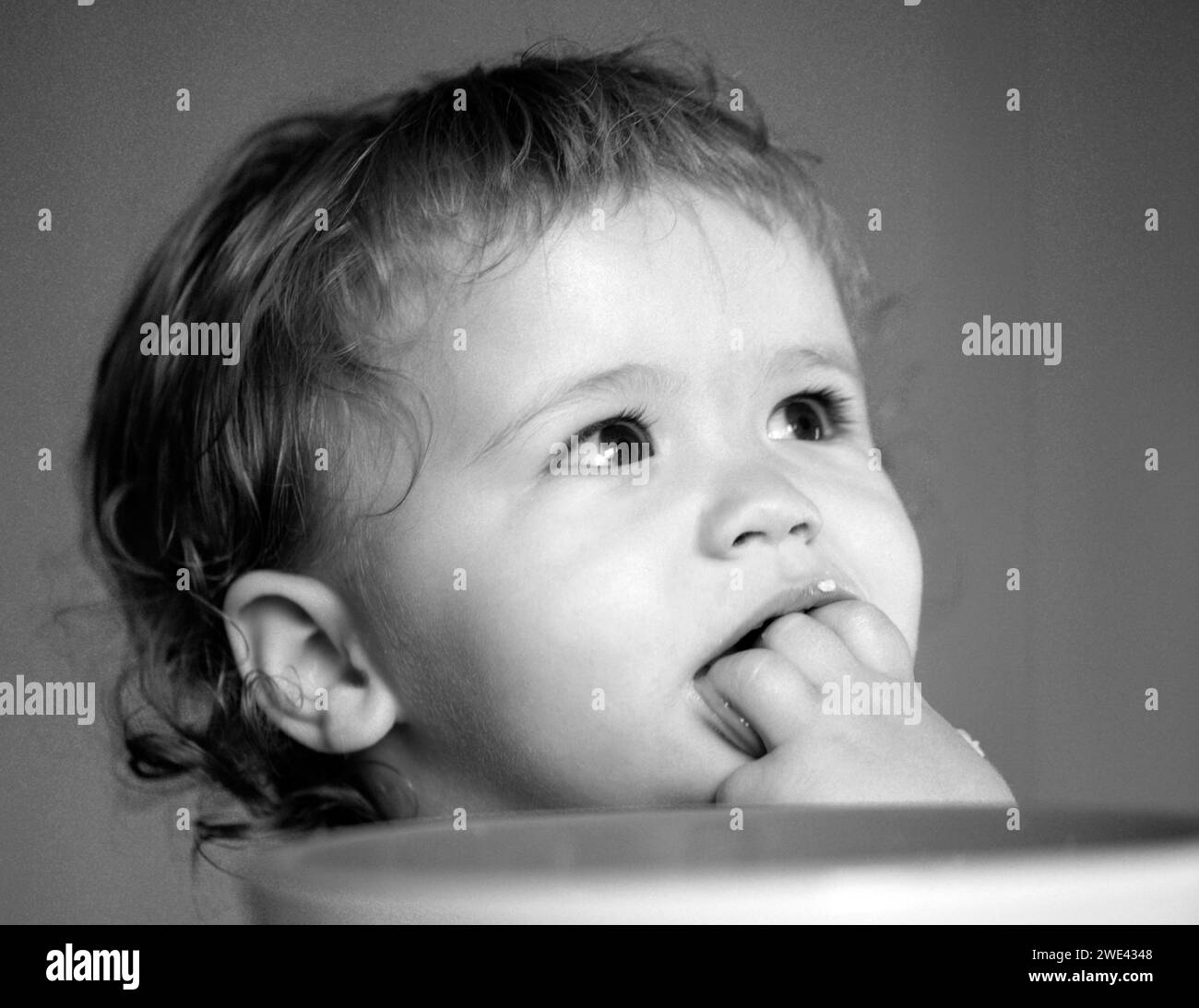 Funny baby eating food himself with a spoon on kitchen. Lick tasty ...
