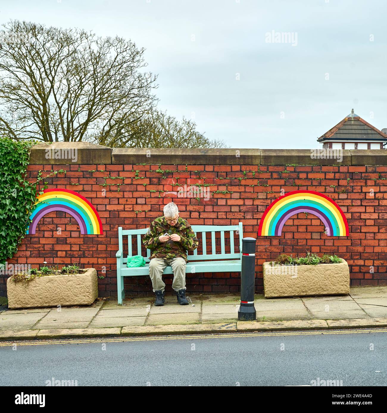 Man sat on street bench between rainbows connected to brick wall Stock ...