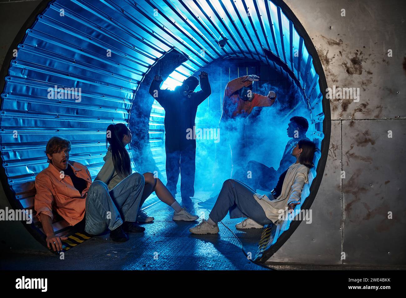 multiethnic friends sitting in tunnel near freaky people in gas masks ...