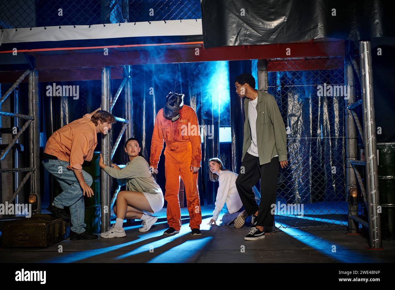 freaky person in orange ppe suit and gas mask near group of interracial ...