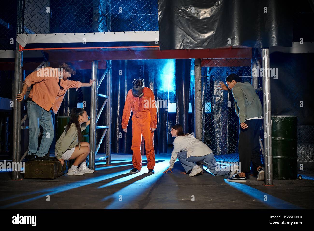 freaky person in orange ppe suit and gas mask near young interracial ...
