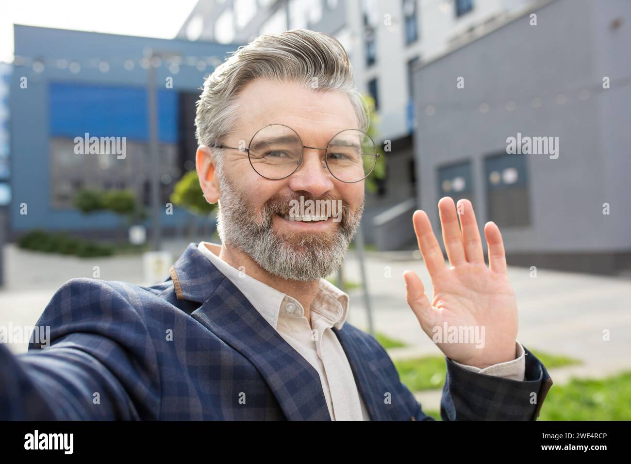 Experienced senior businessman in a sharp suit waving hello outside an ...