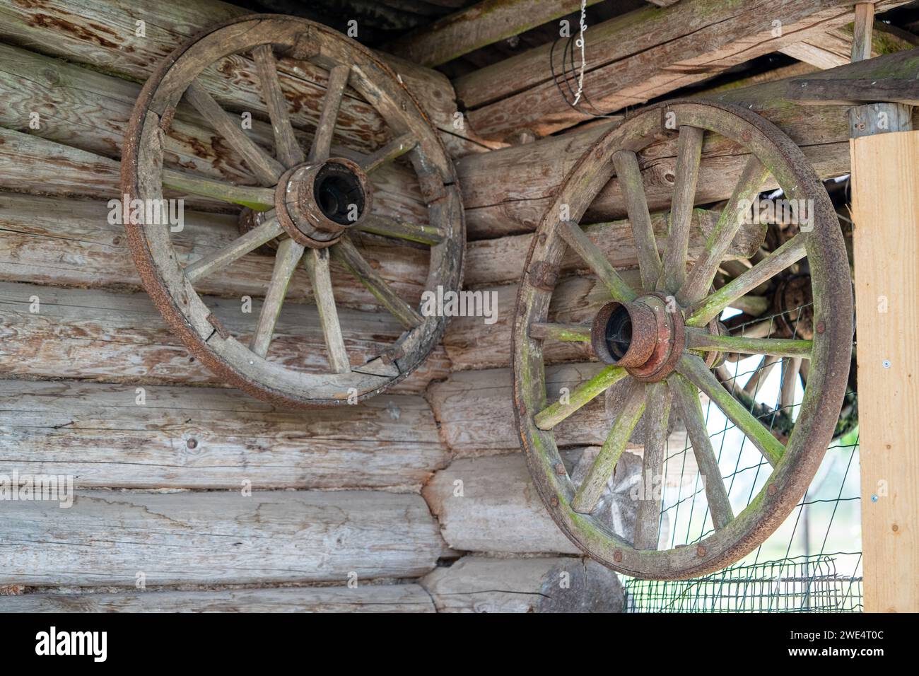 An old wooden cart wheels hang on the log wall of a village house Stock ...
