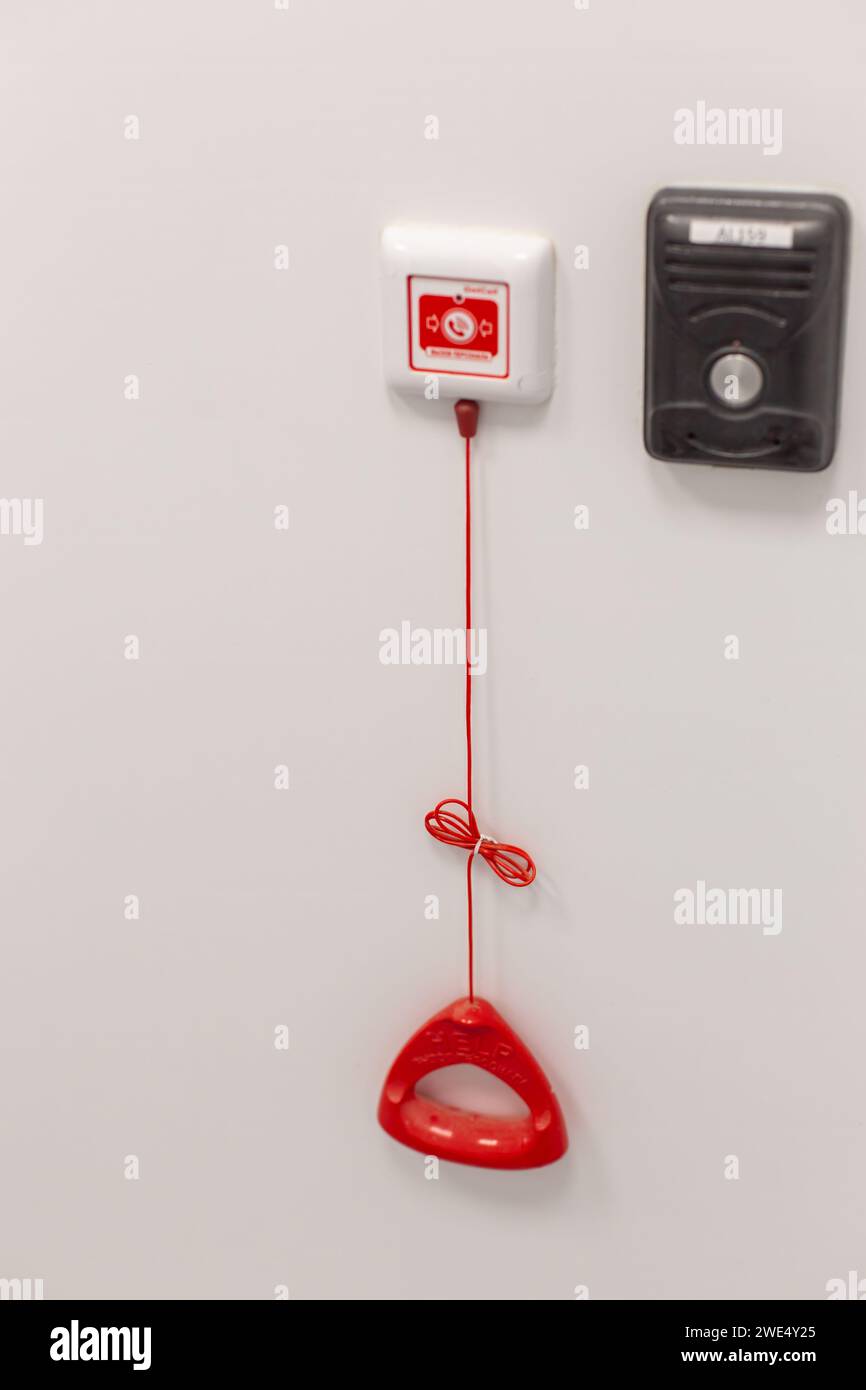 A red emergency pull cord system on a white wall in a clinical setting ...