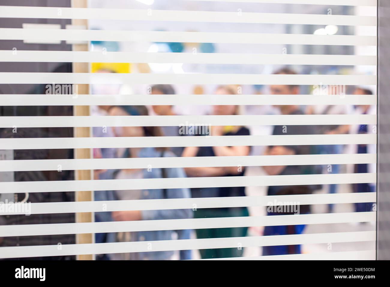 Blurred figures of people seen through the slats of window blinds ...