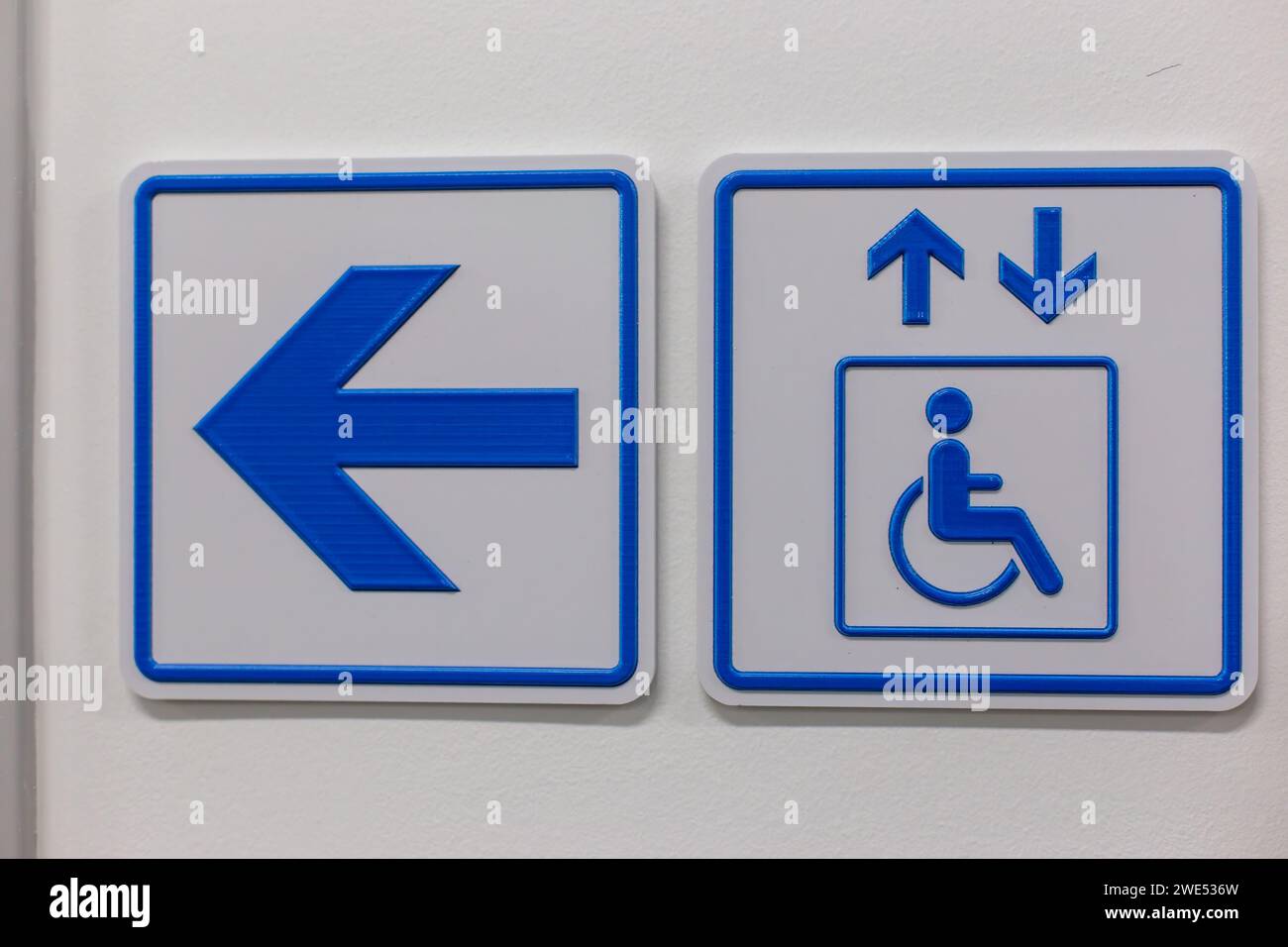 A blue arrow and elevator access signs disabled person on the wall Stock Photo - Alamy