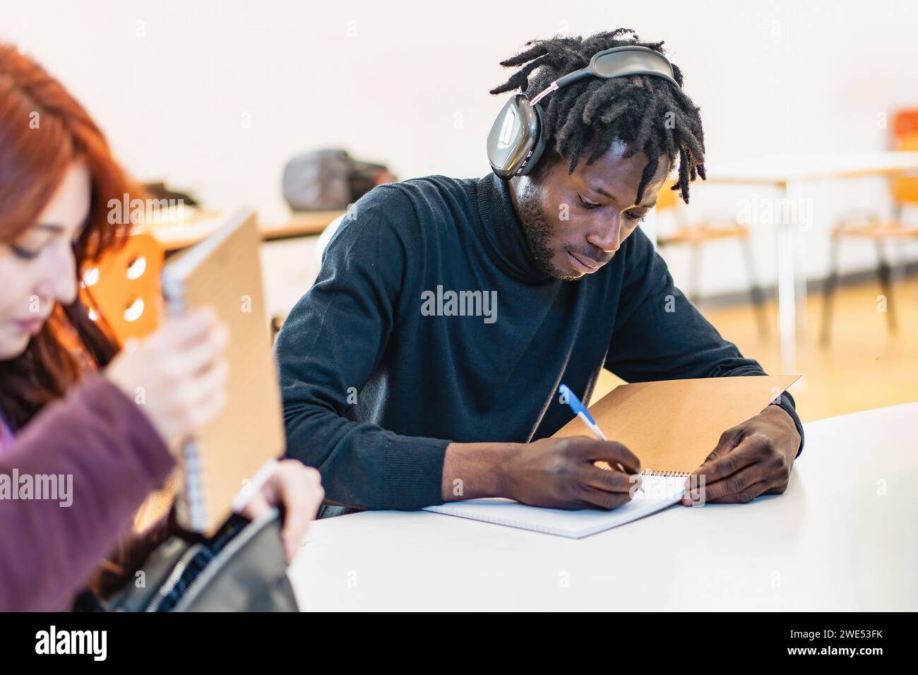 Young African male student with headphones intently writing notes at a ...