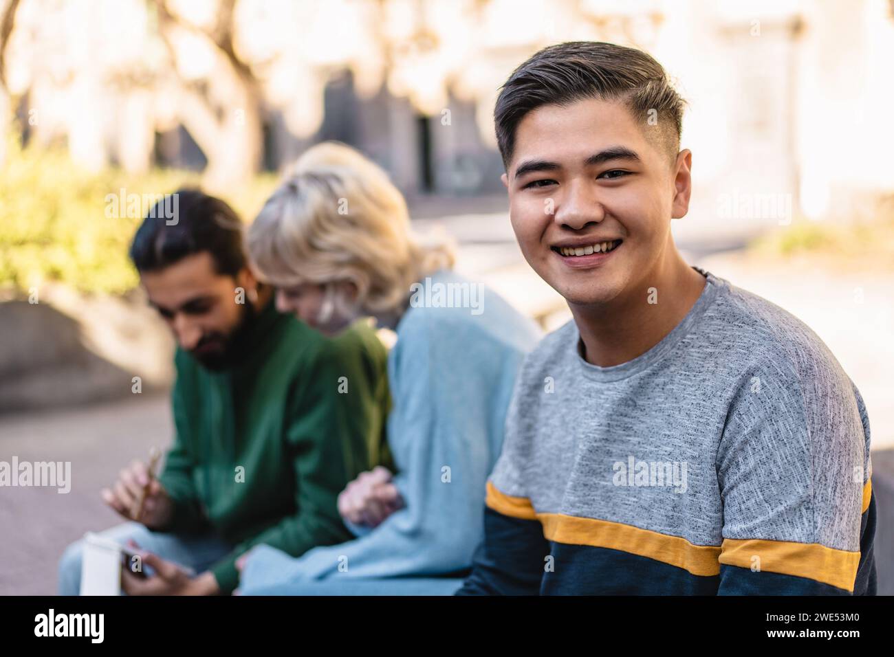 Portrait of a cheerful young Asian male student with friends in a blur ...