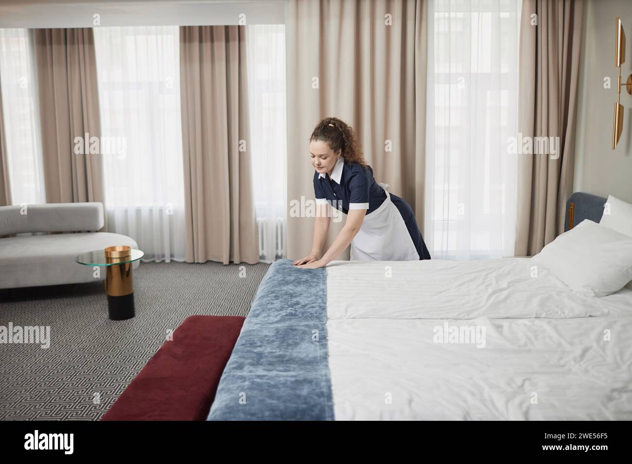 Wide angle view at young housekeeper cleaning hotel room and making ...