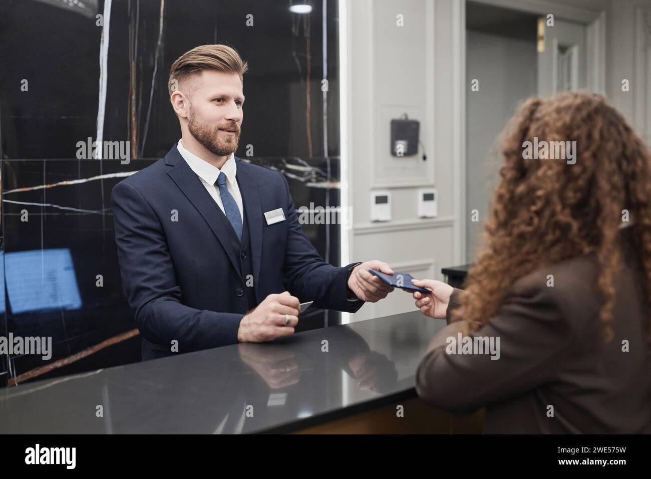 Portrait of young man working at hotel reception desk and taking ...