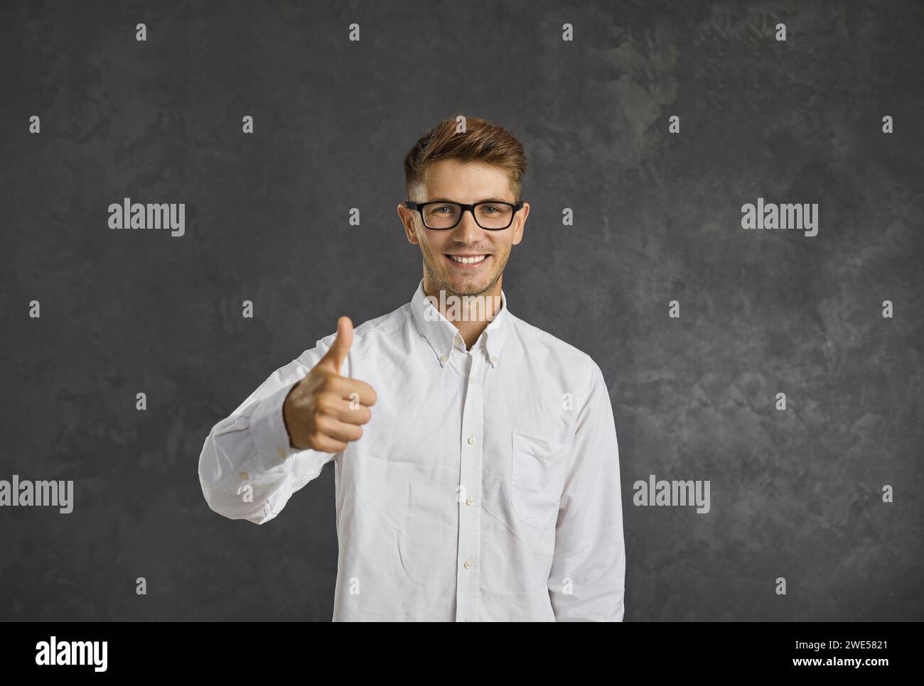 Happy young man in glasses giving thumbs up standing isolated on grey ...