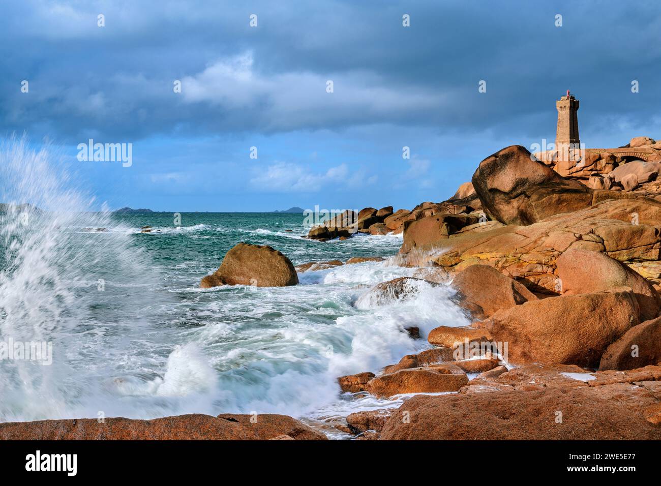 Surf hits pink granite rocks, Phare de Men Ruz lighthouse in background ...