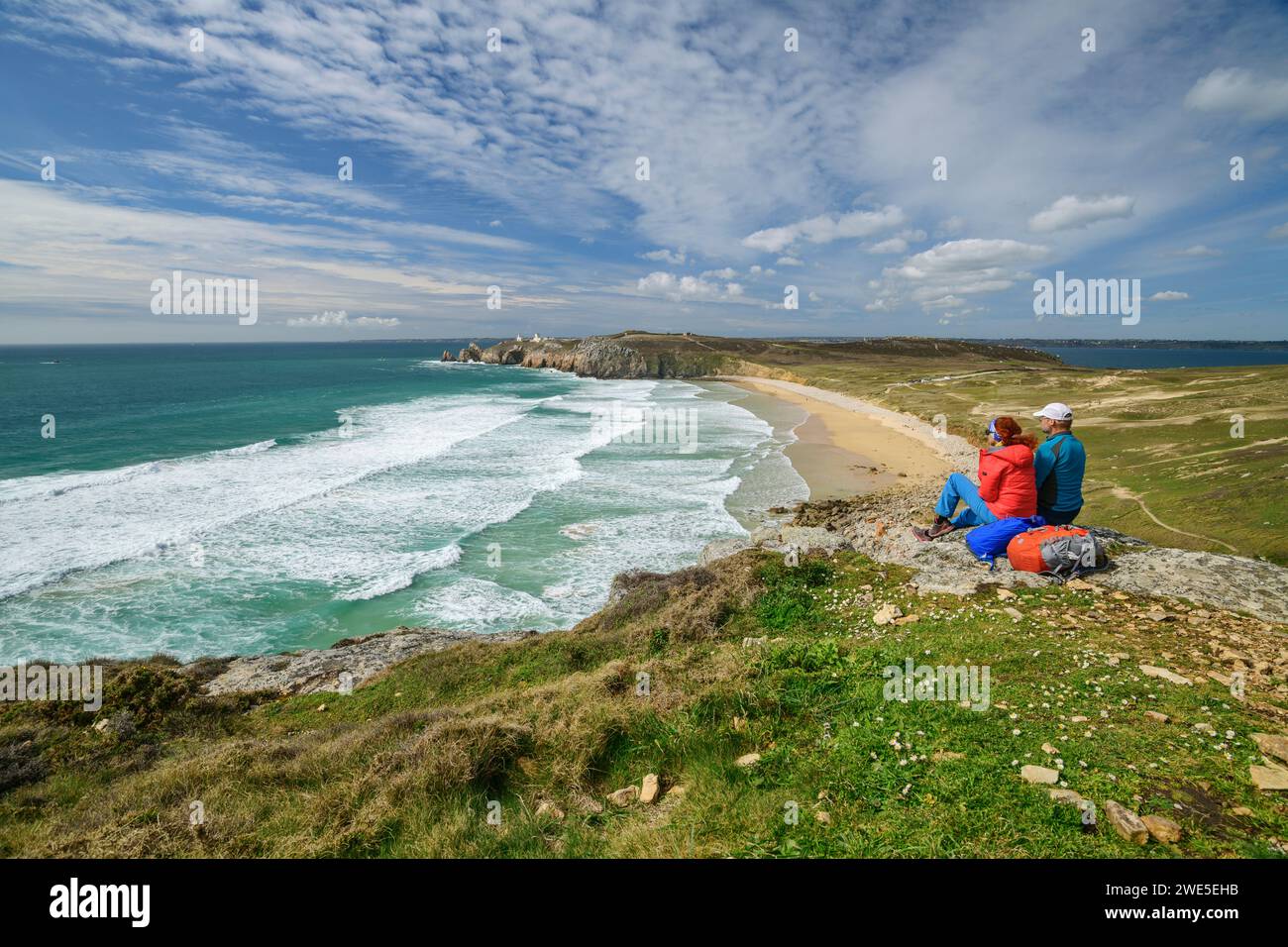 Man and woman hiking sitting on rocks and looking at Plage de Pen Hat ...