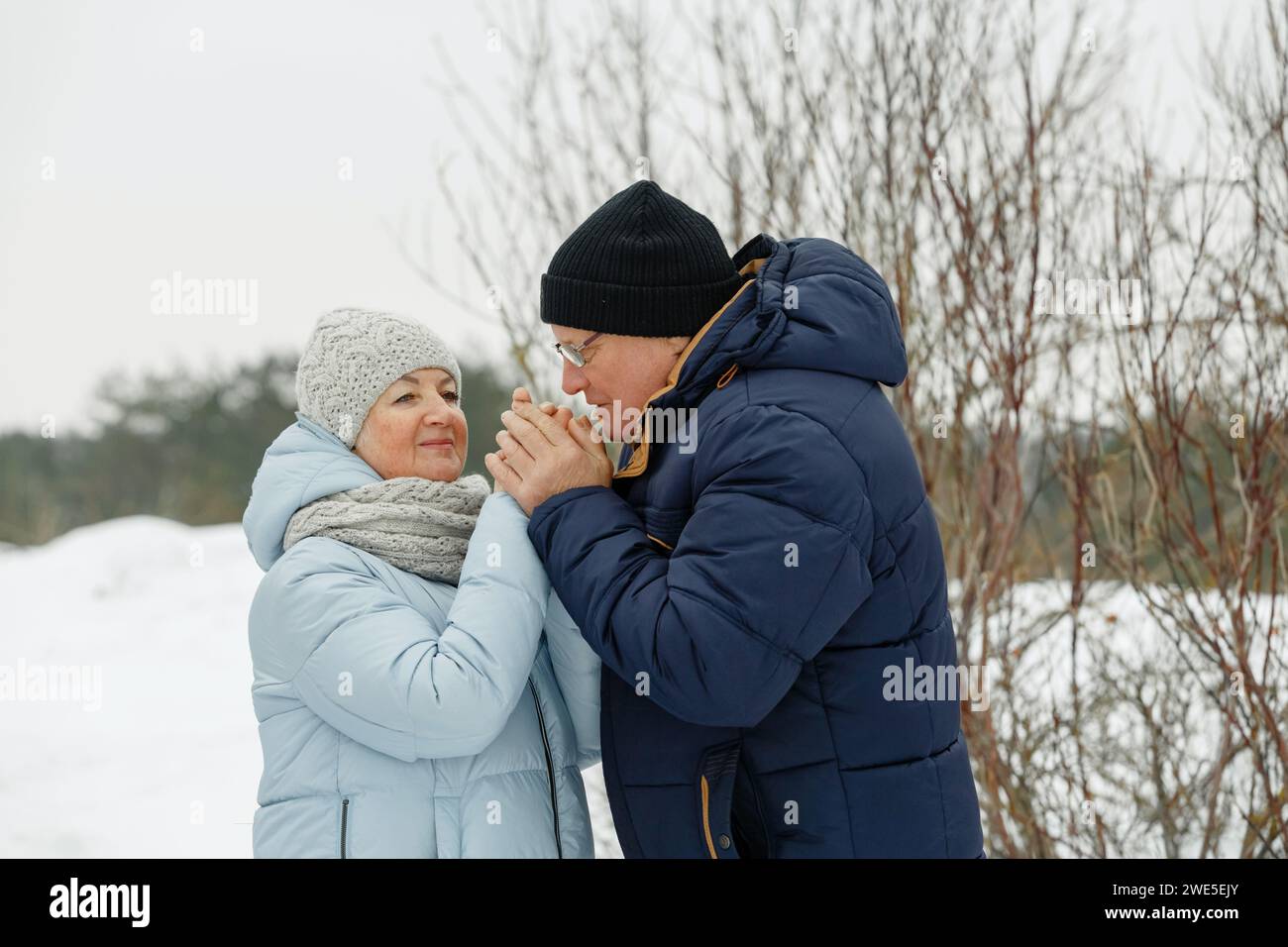An elderly caring man warms his wife's hands with his breath on the ...