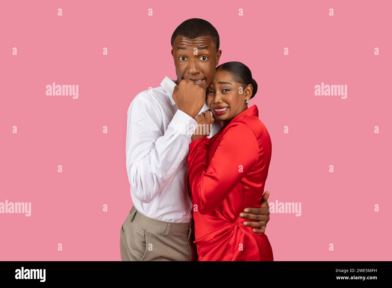 Scared black man hugging woman, couple elegant attire, pink background ...