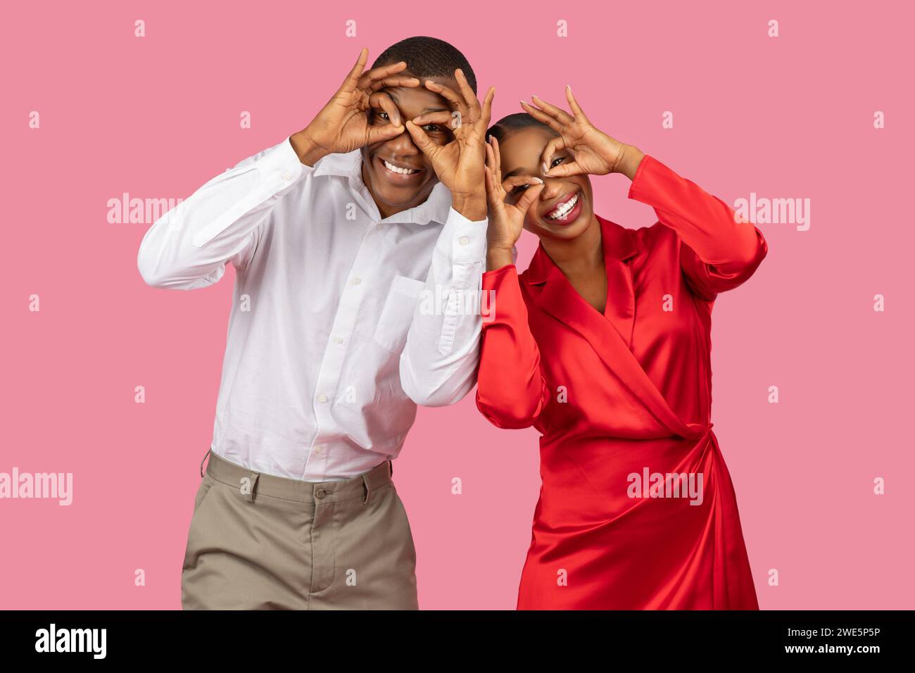 Couple making fun hand gestures over eyes, playful poses, pink ...