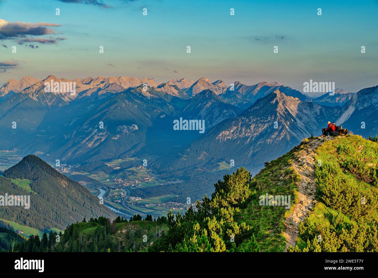 Two people hiking sit on a viewing bench and look at the Karwendel and ...