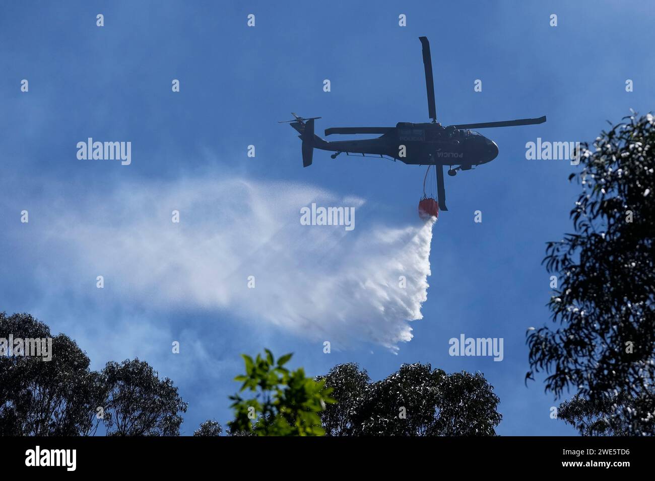 A helicopter sprays water on a wildfire fire in the mountains ...